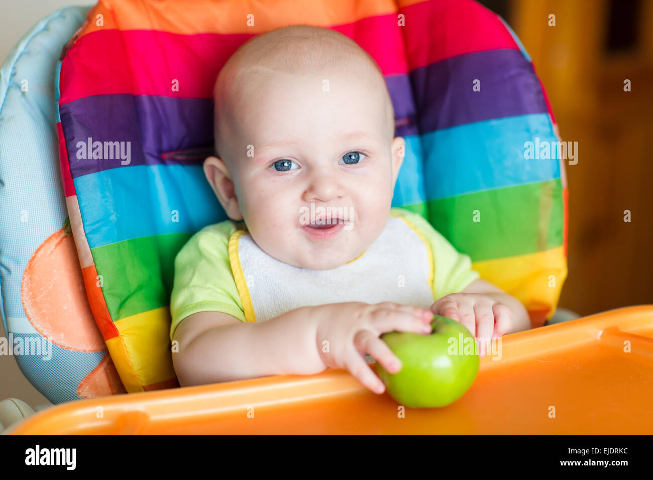 Adorable baby eating apple in high chair. Baby's first solid food Stock ...