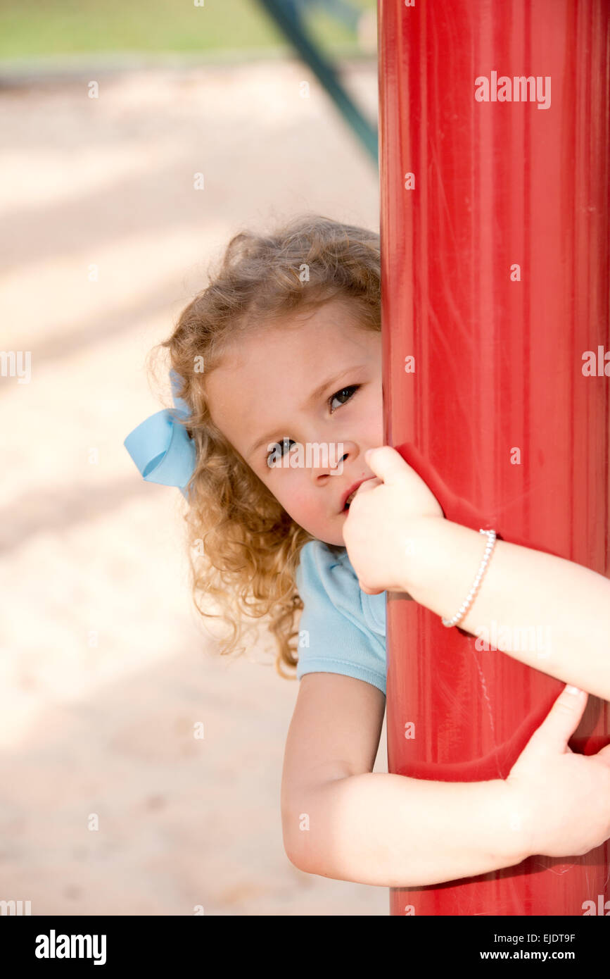 Four year old girl playing at park playground and hugging a red pole ...