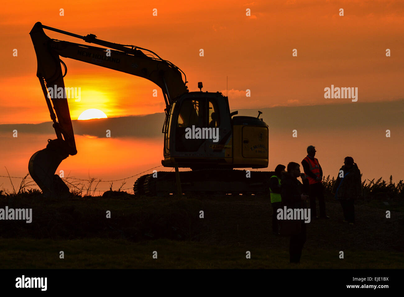 Mechanical digger and workers silhouetted again the evening sun ...