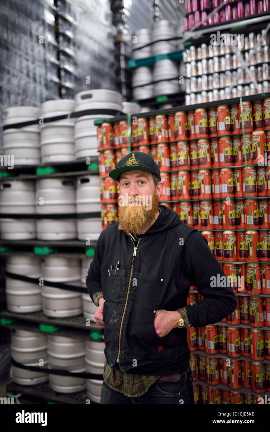 Brewery worker standing at stacks of cans and stainless steel barrels ...