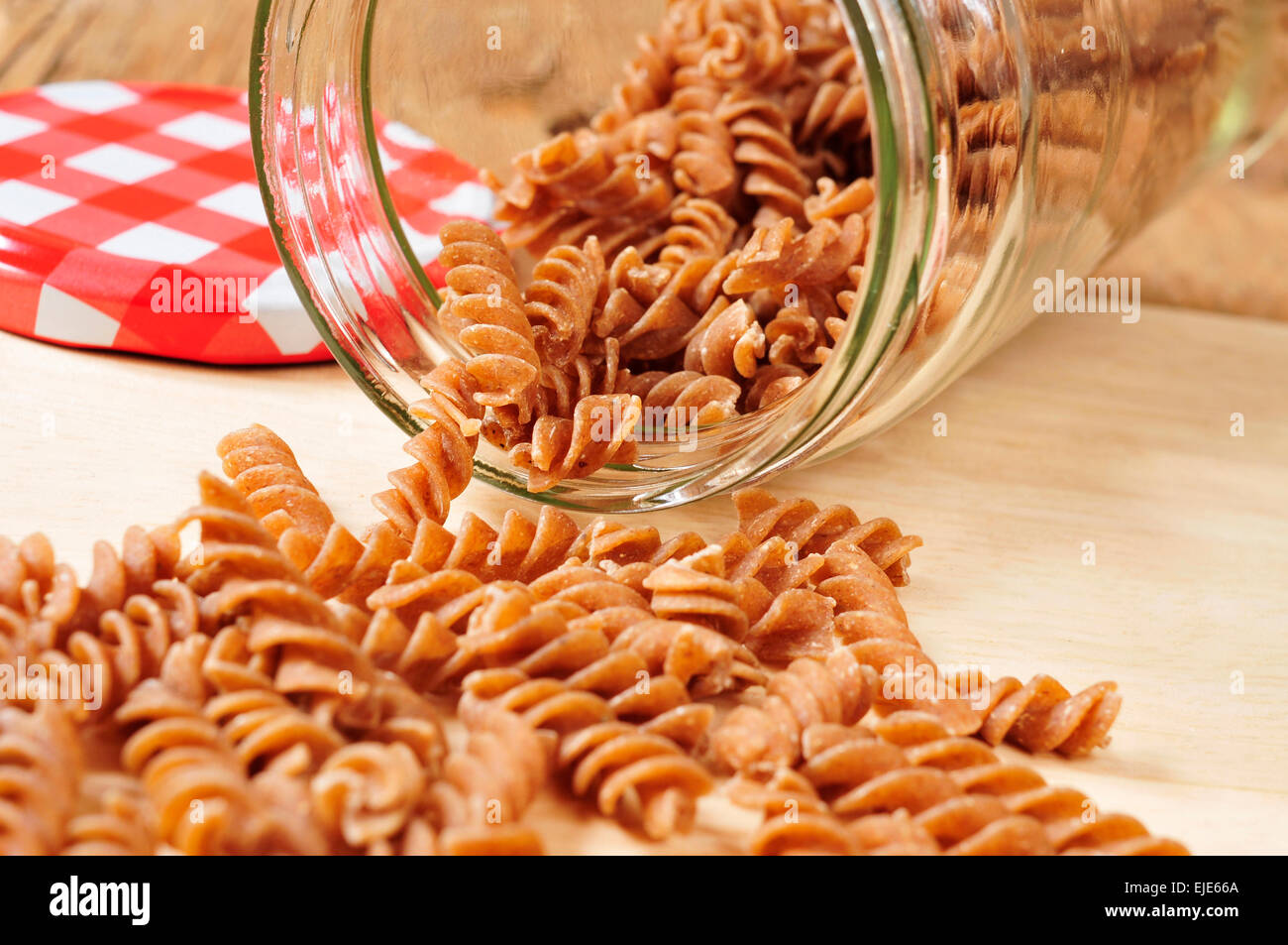 closeup of a pile of uncooked spelt fusilli coming out of a glass jar ...