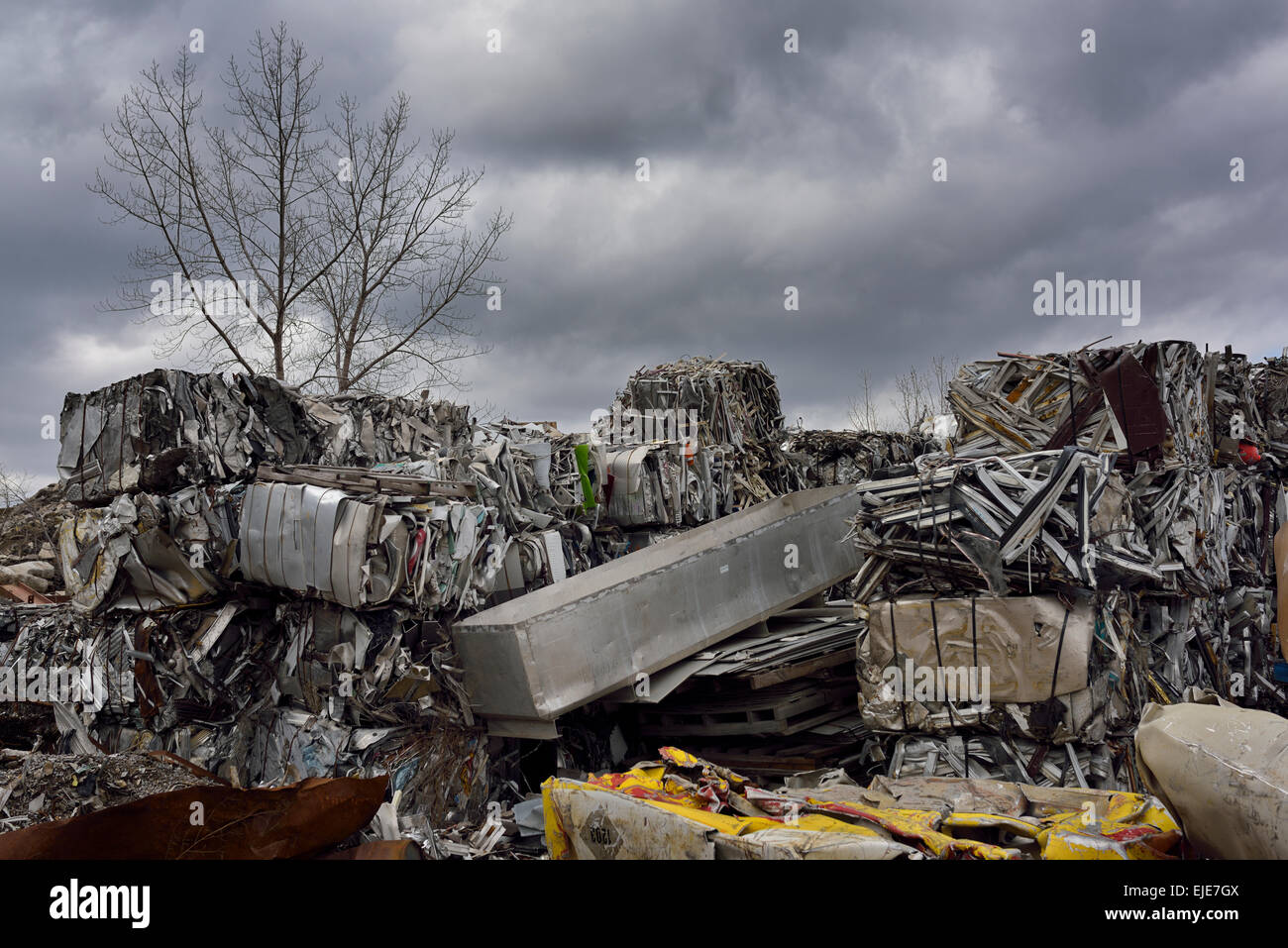 Heap of cubes of crushed recycled scrap metal junk with clouds and tree ...