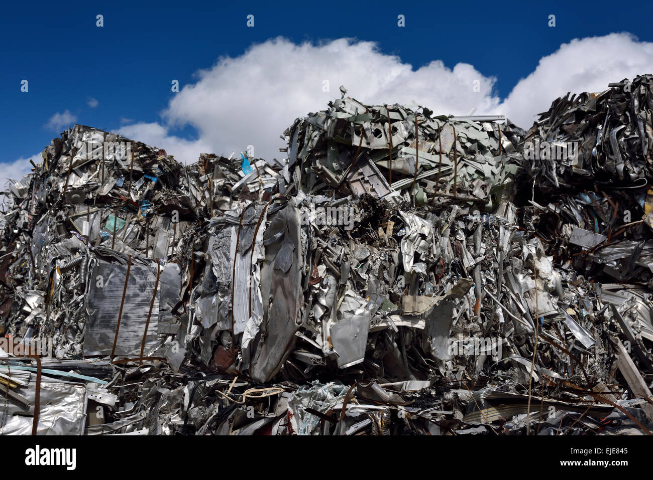 Bales of crushed recycled scrap metal in junkyard with blue sky clouds ...