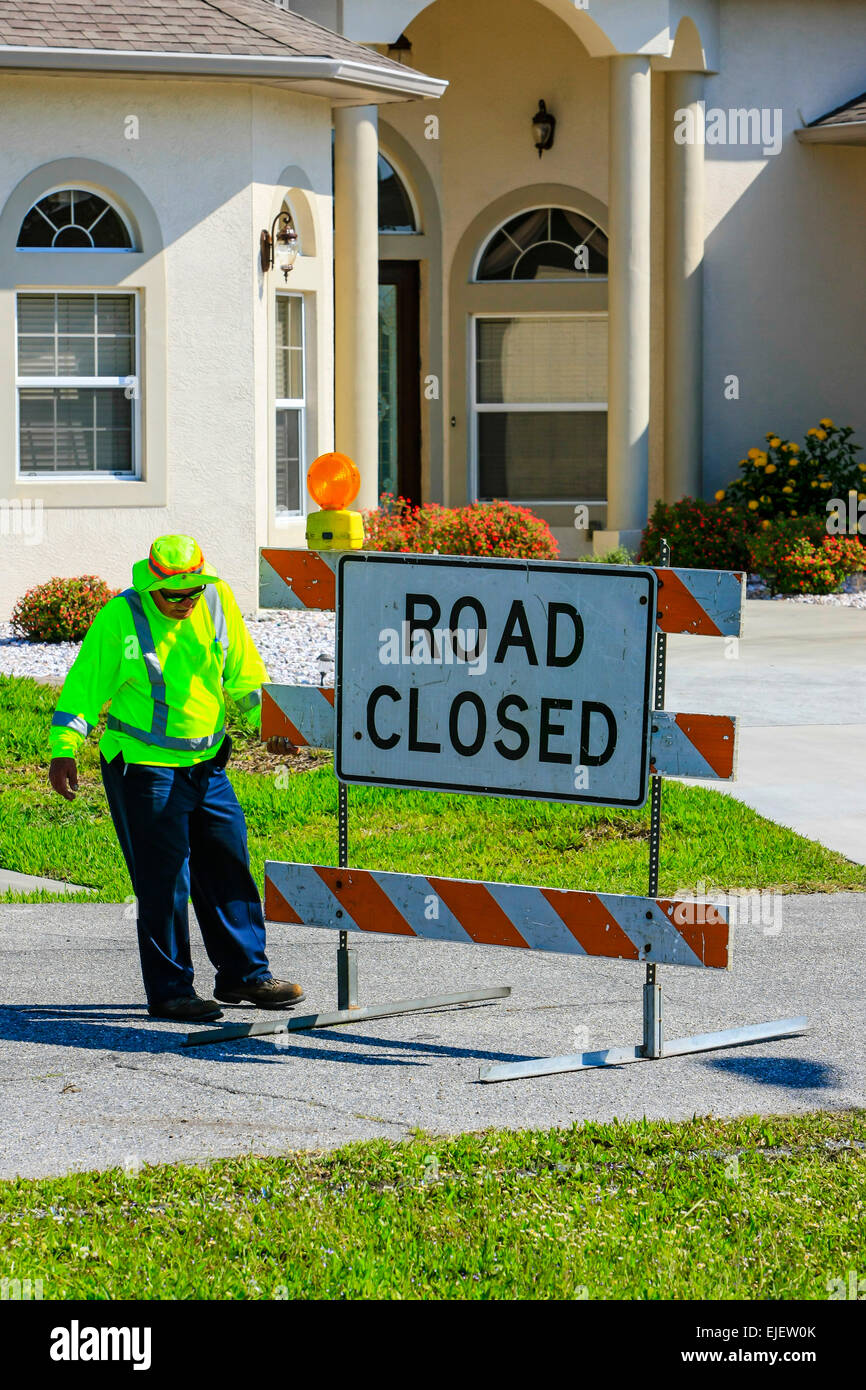 Road maintenance worker moves a "Road Closed" sign across a residential ...