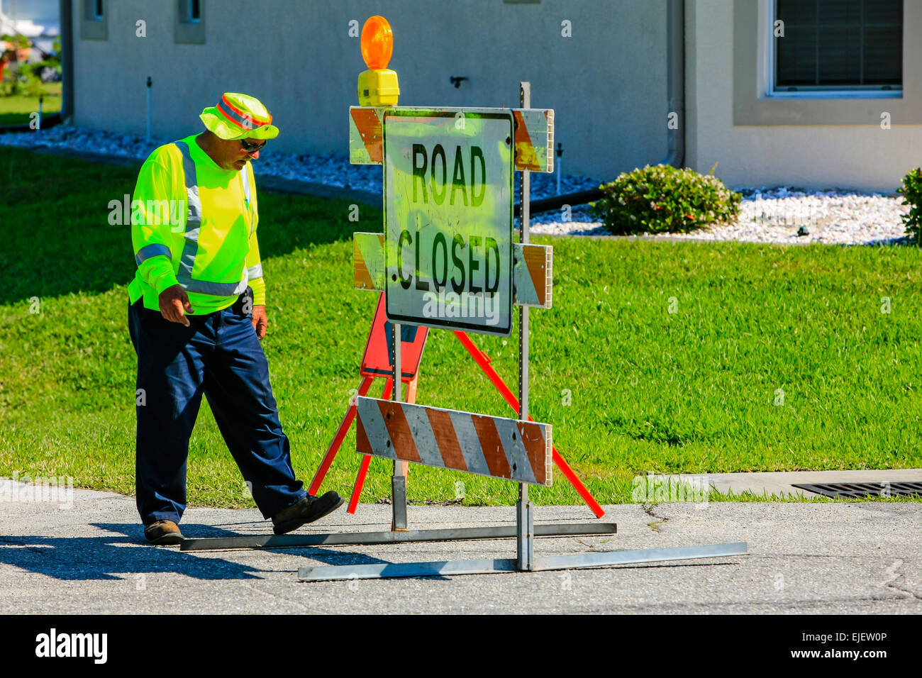 Road maintenance worker moves a "Road Closed" sign across a residential ...