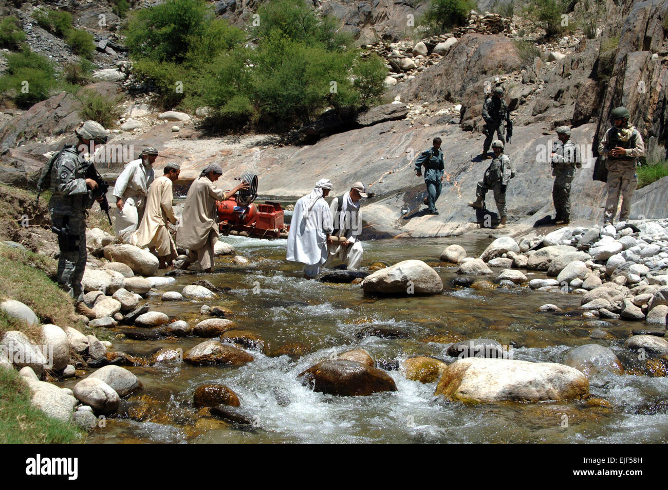 Road construction workers cross a stream while Afghanistan national ...