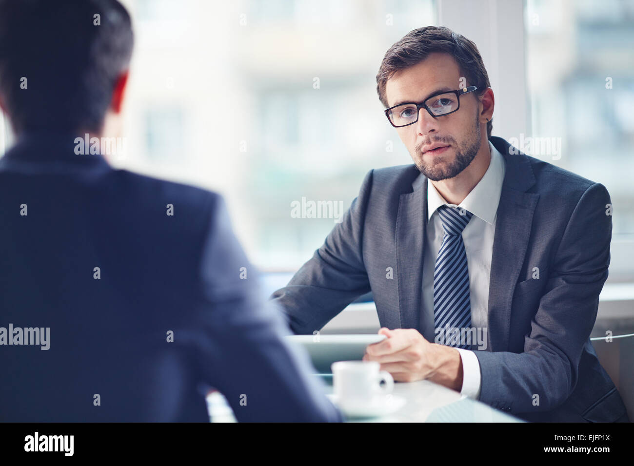 Serious businessman looking at camera at workplace with his colleague ...