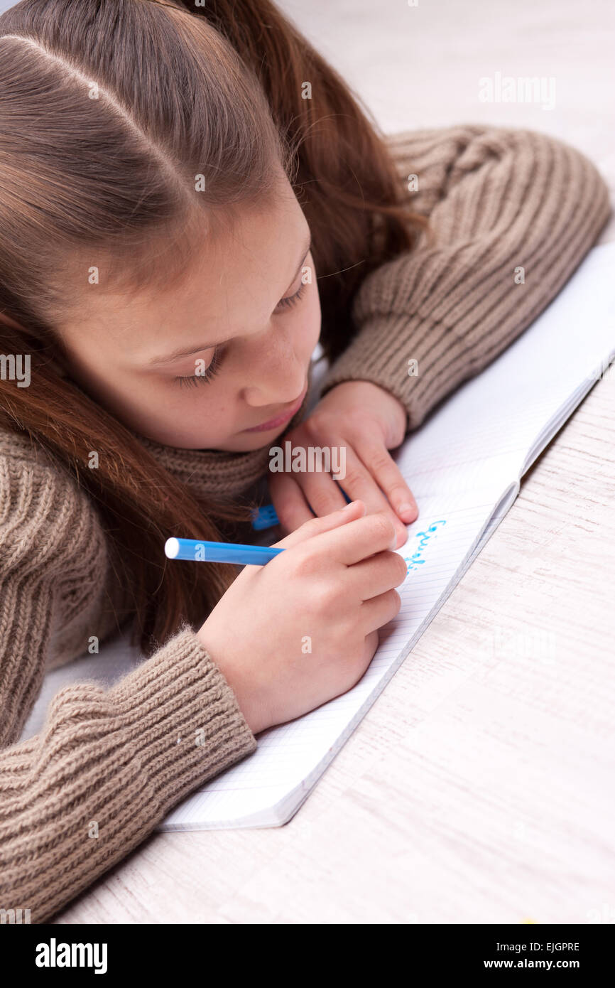 little girl on the floor writing concentrated on her exercise book with ...