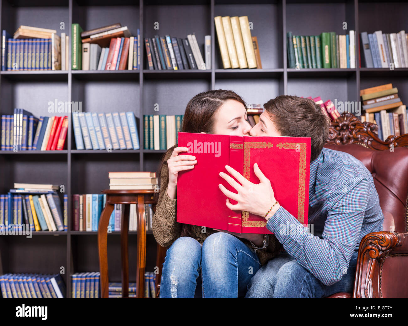 Romantic Young Couple Sneaking A Kiss As They Sit Reading In A Library