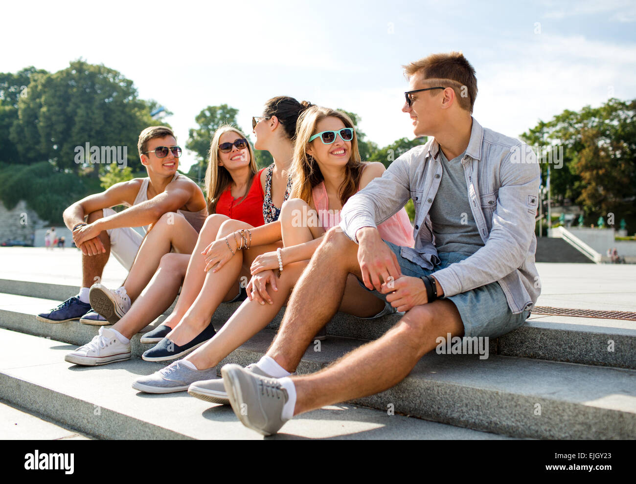 group of smiling friends sitting on city street Stock Photo - Alamy