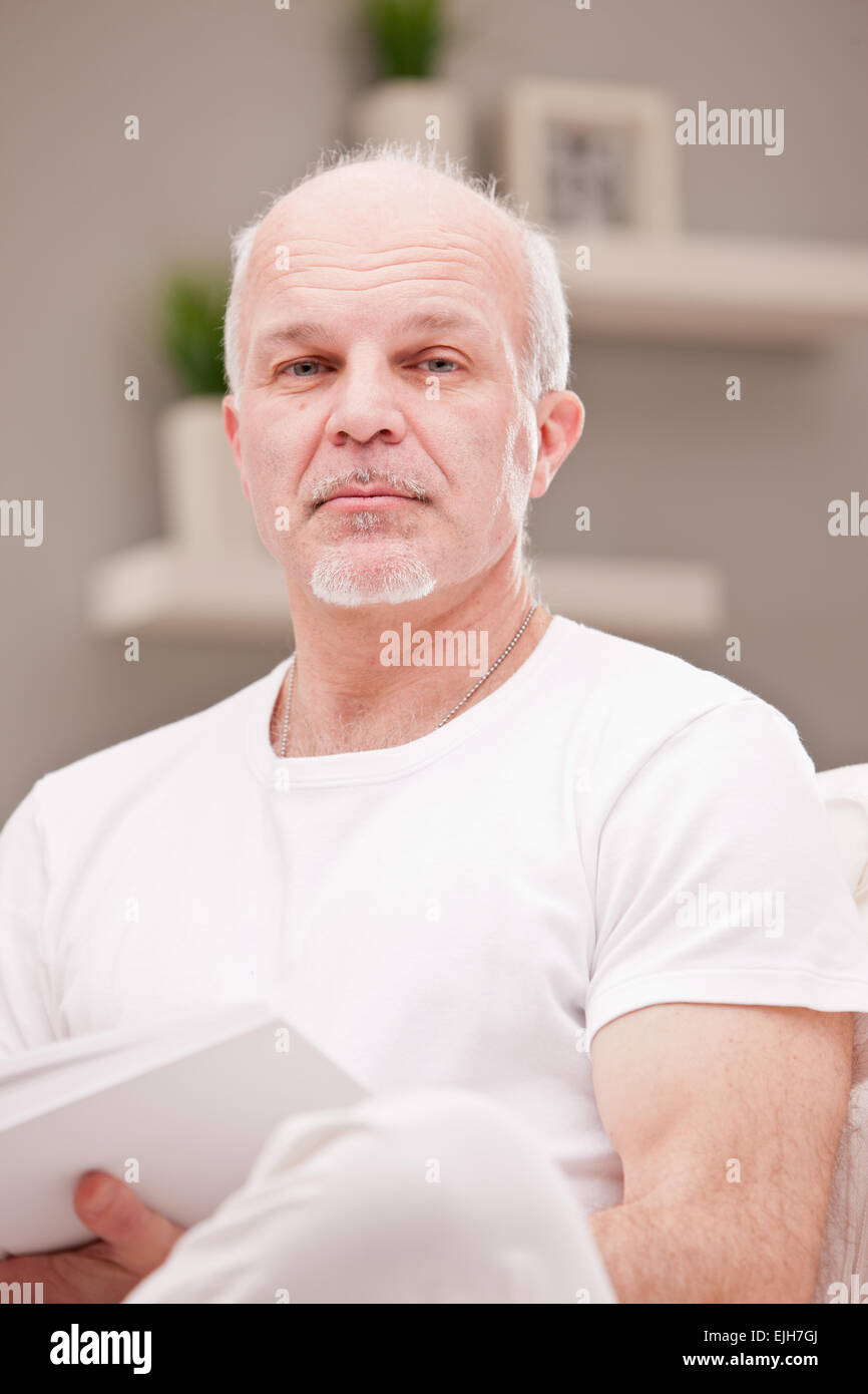 serious portrait of a tired man in his living room trying to read a ...