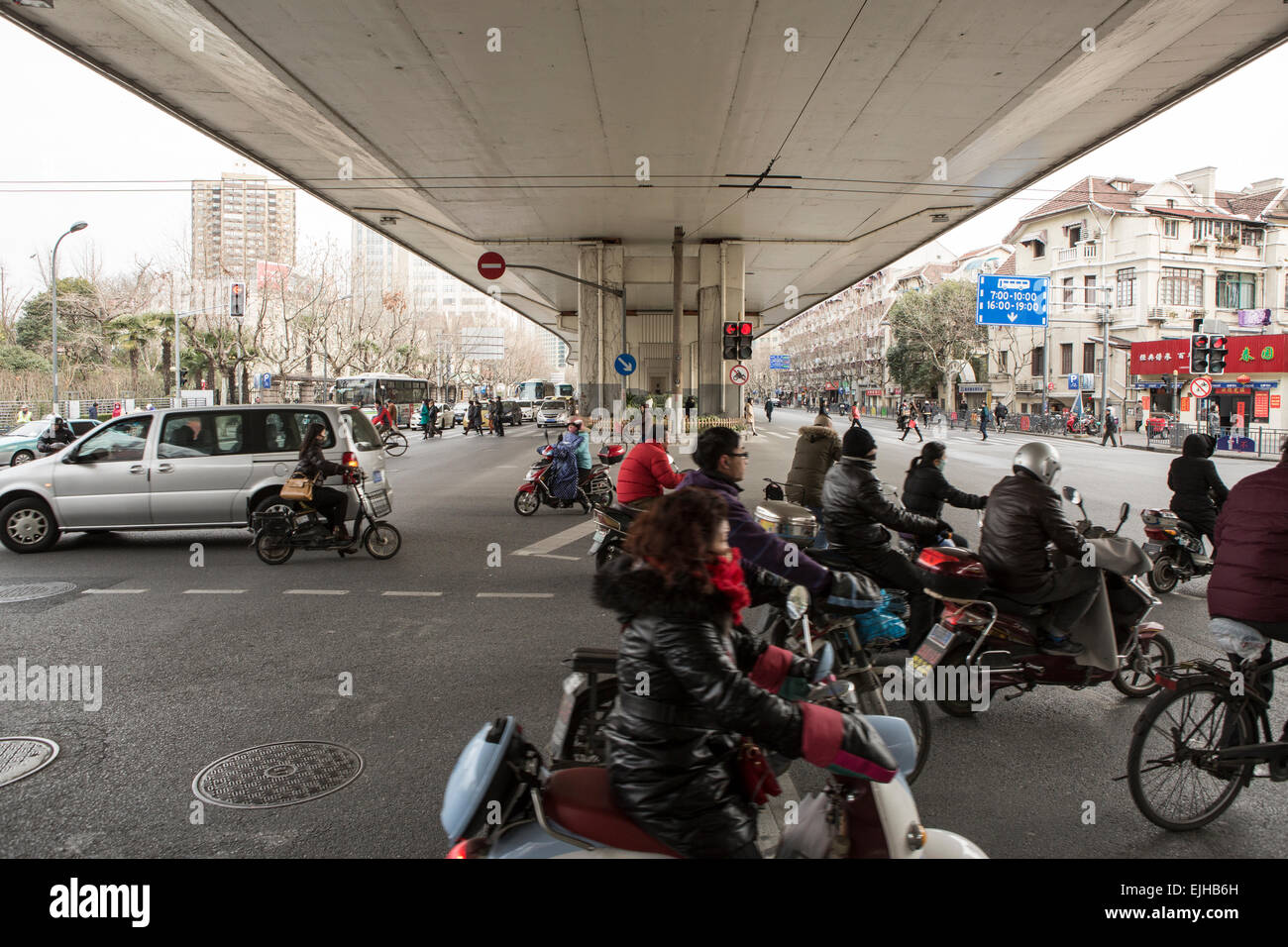 Commuters on motorbikes and scooters under a highway in Shanghai, China ...