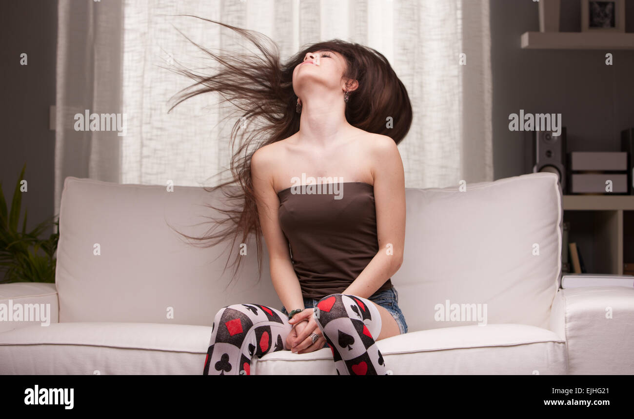 hair in the air by a young pretty woman in her living room on a couch ...