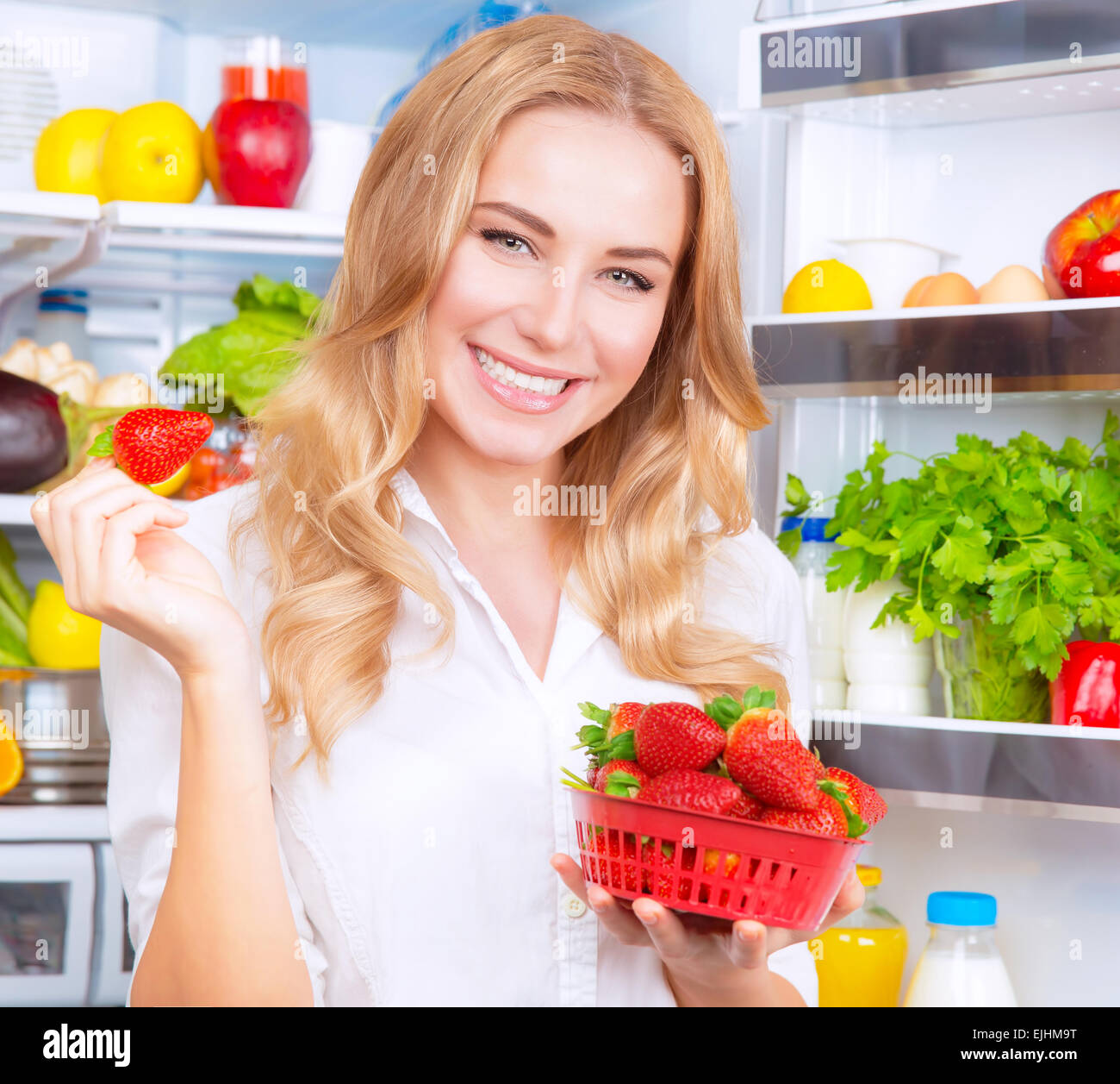 Closeup portrait of a beautiful female eating strawberry, standing next ...