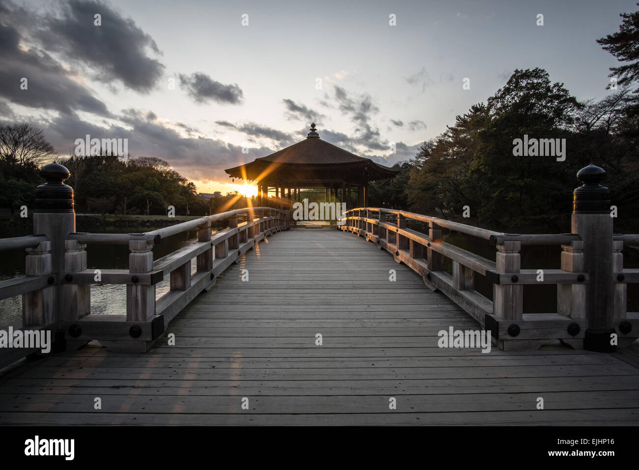 Sun setting behind a wooden Japanese building at the end of a bridge ...