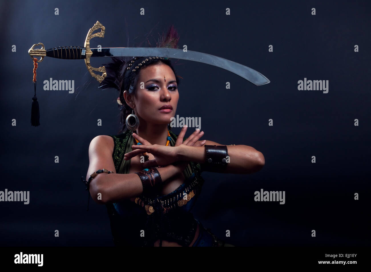 Studio shot of Asian belly dancer balancing a sword on her head with ...