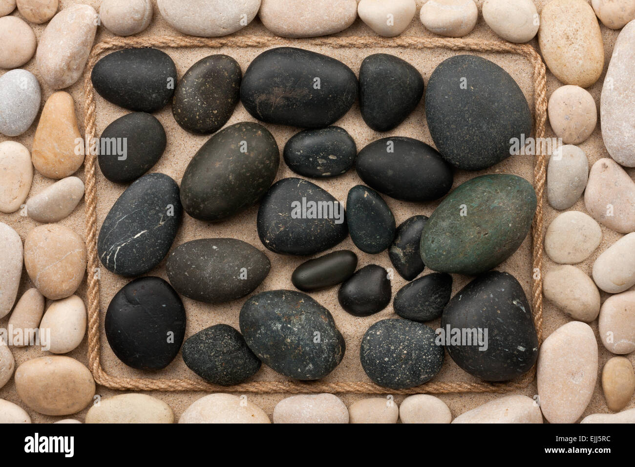 Beautiful frame made of rope with black and white stones on the sand ...