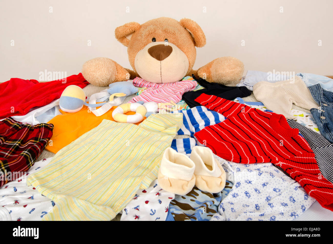 Bear toy on a bed with different colorful new born clothes.Colorful ...