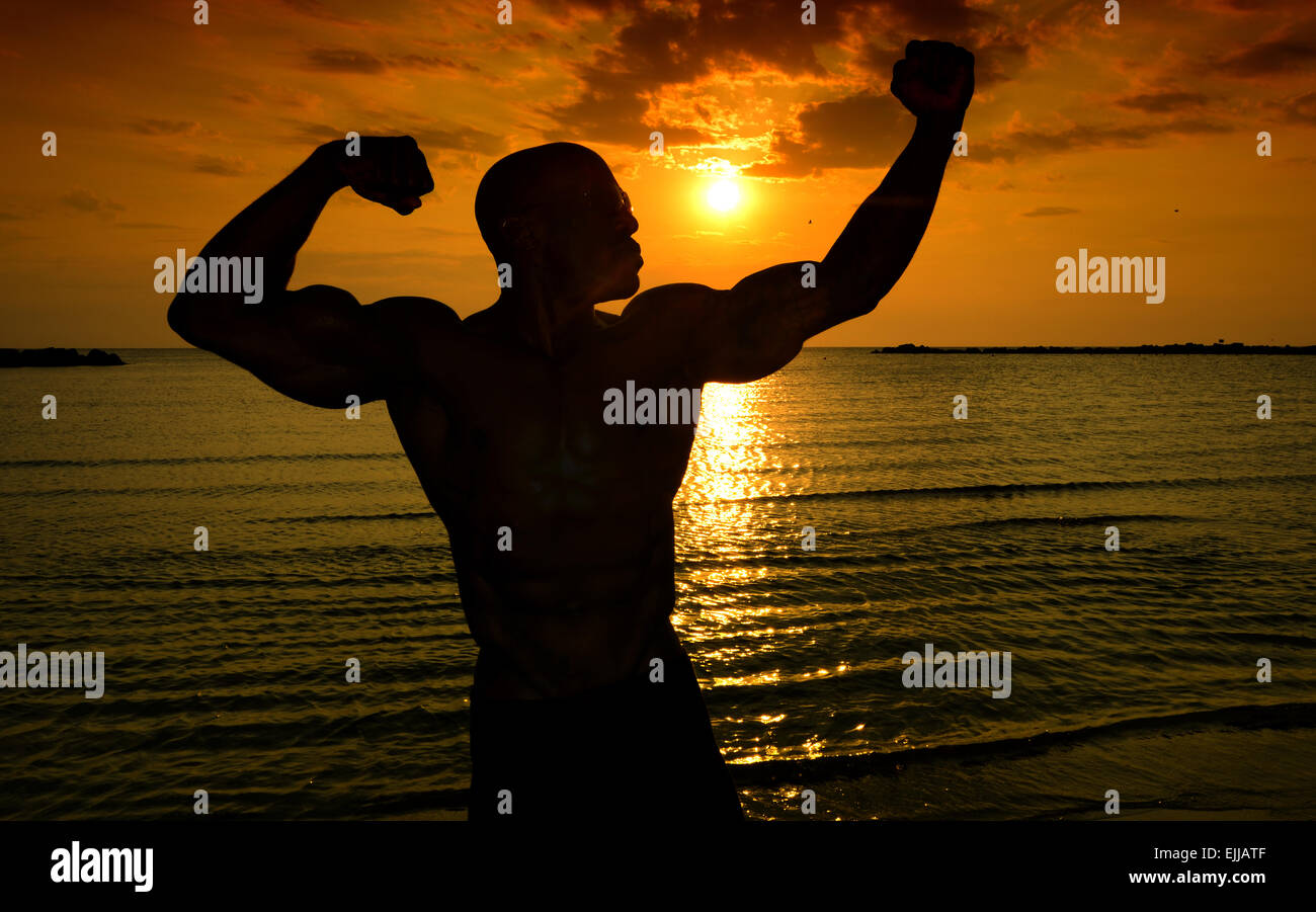 Silhouette of bodybuilder posing at the sunrise on the beach, training ...