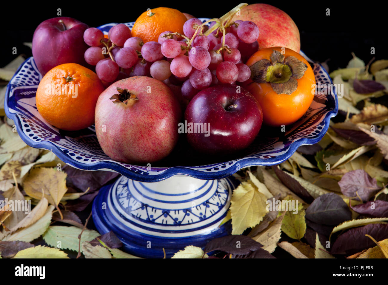 Ceramic fruit bowl with autumn fruits isolated over black background ...