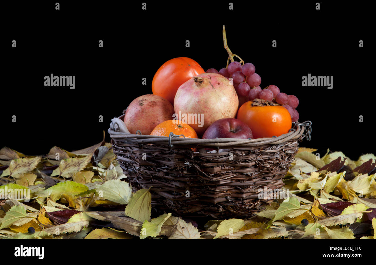 Old basket fruit bowl with autumn fruits isolated over black background ...