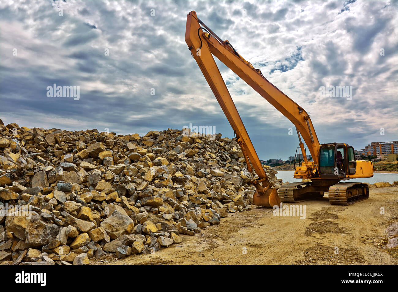 Yellow excavator and big pile of rocks Stock Photo - Alamy