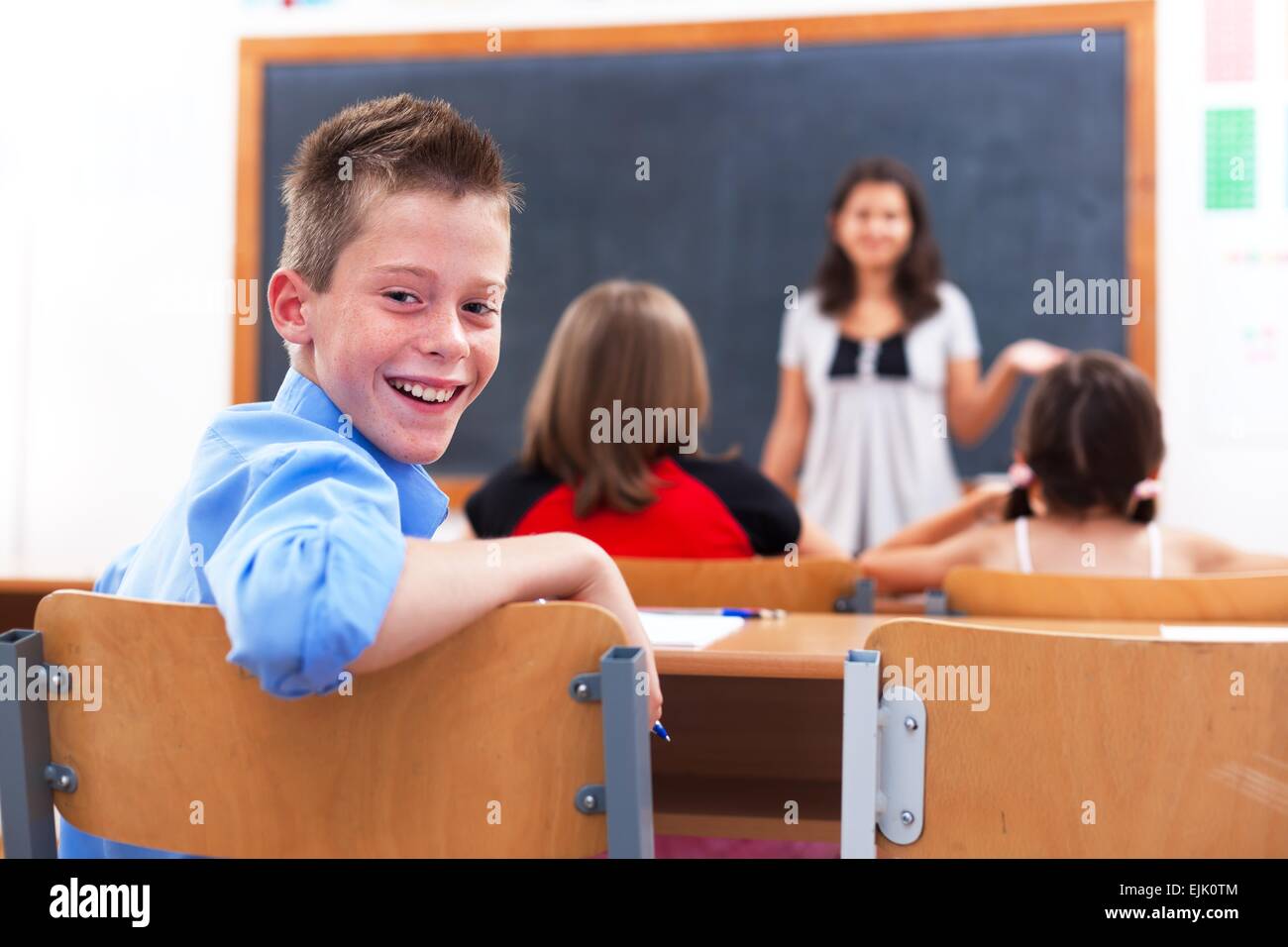 Cheerful school boy looking back in class room while the teacher ...