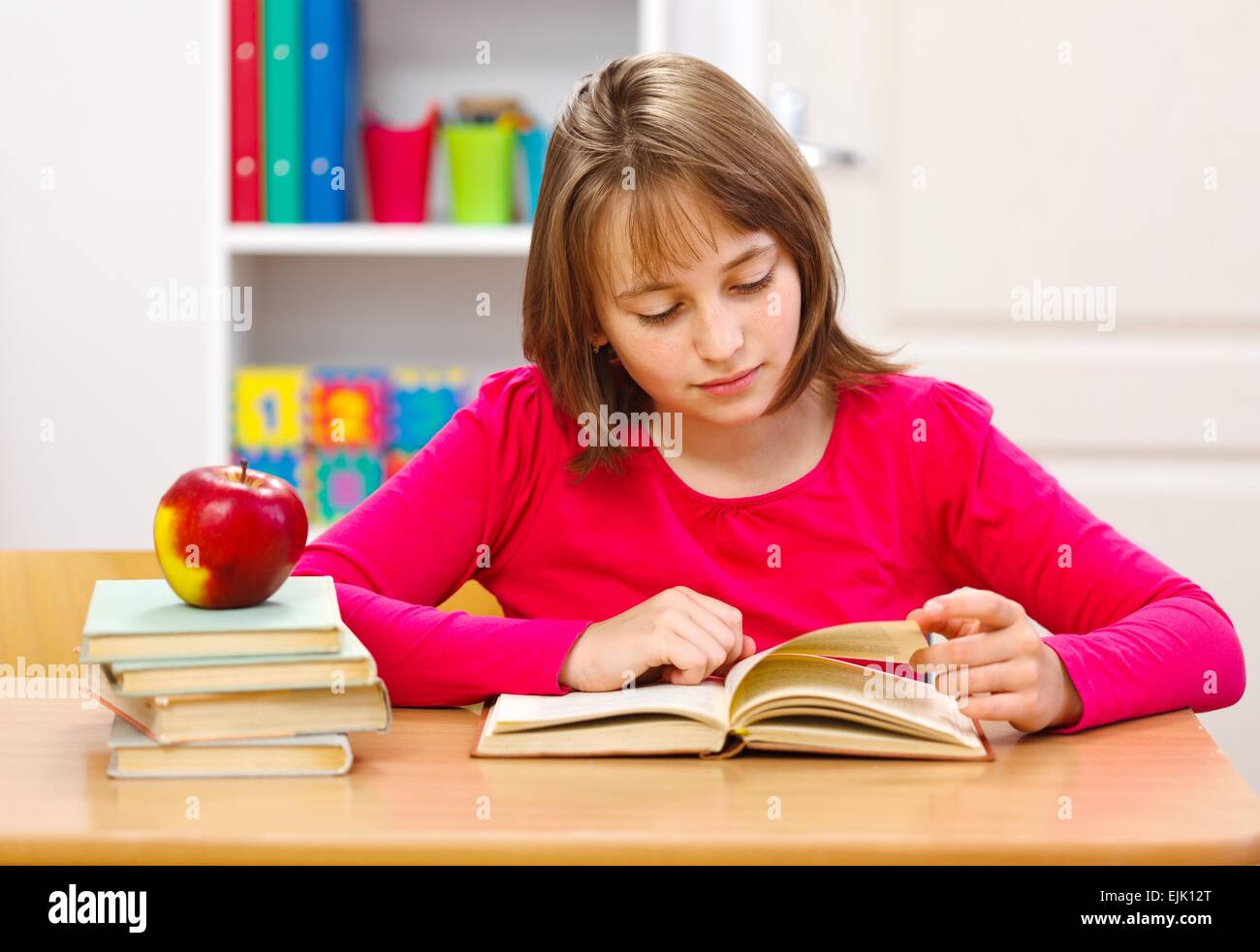 Schoolgirl reading book in classroom. Whole apple on a stack of other ...