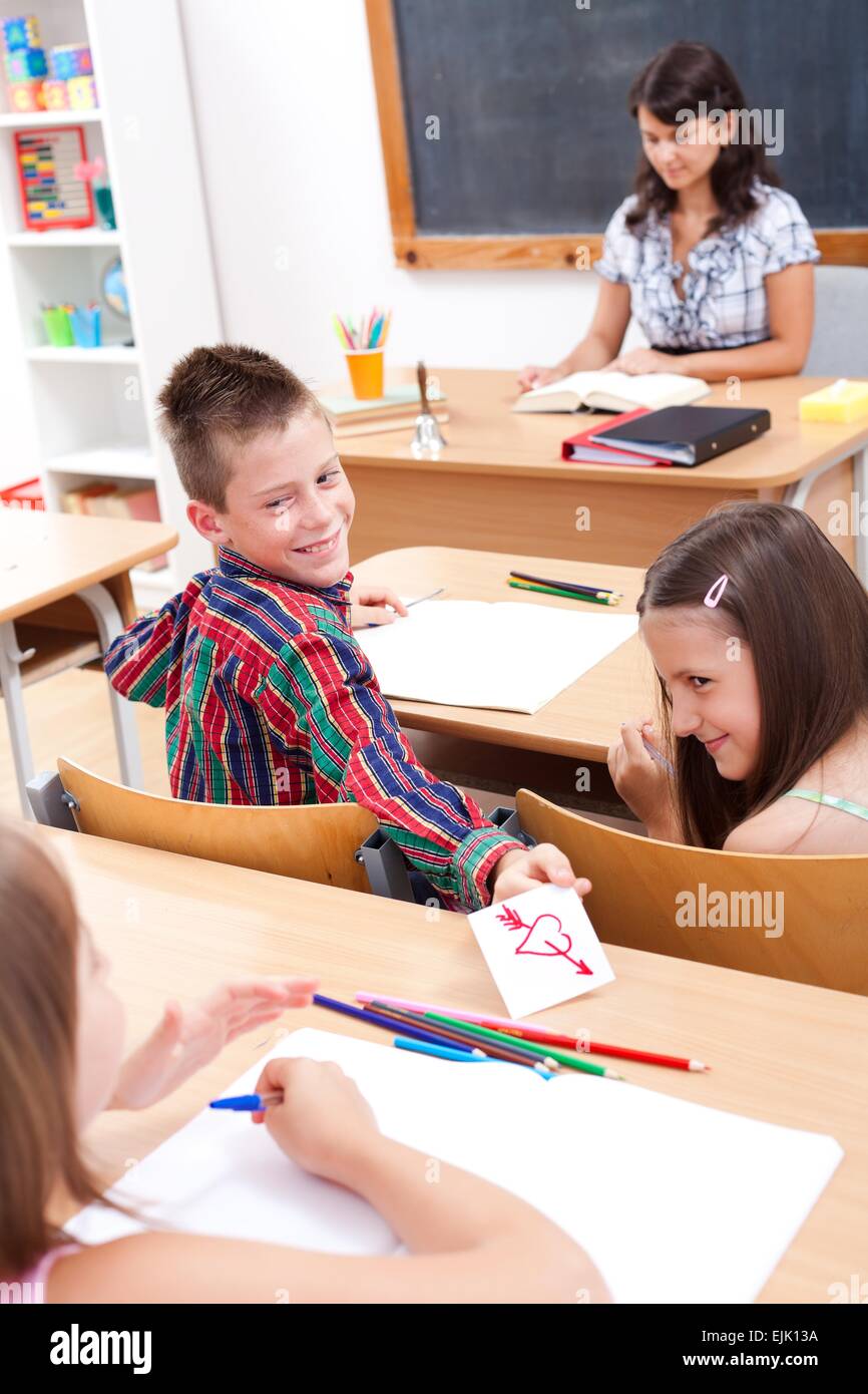Cheerful elementary school boy giving love letter to his classmate ...