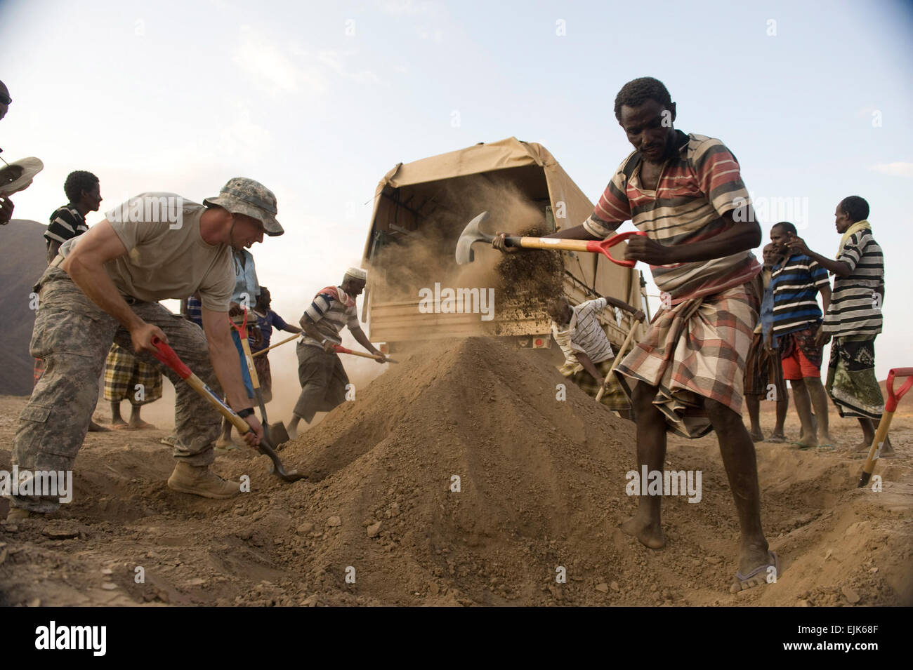 Villagers and U.S. Army soldiers load dirt into a light armored ...