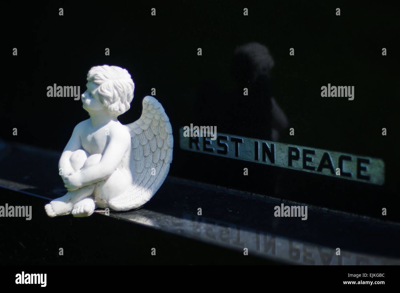 Small angel sitting on plinth of black granite gravestone with ...