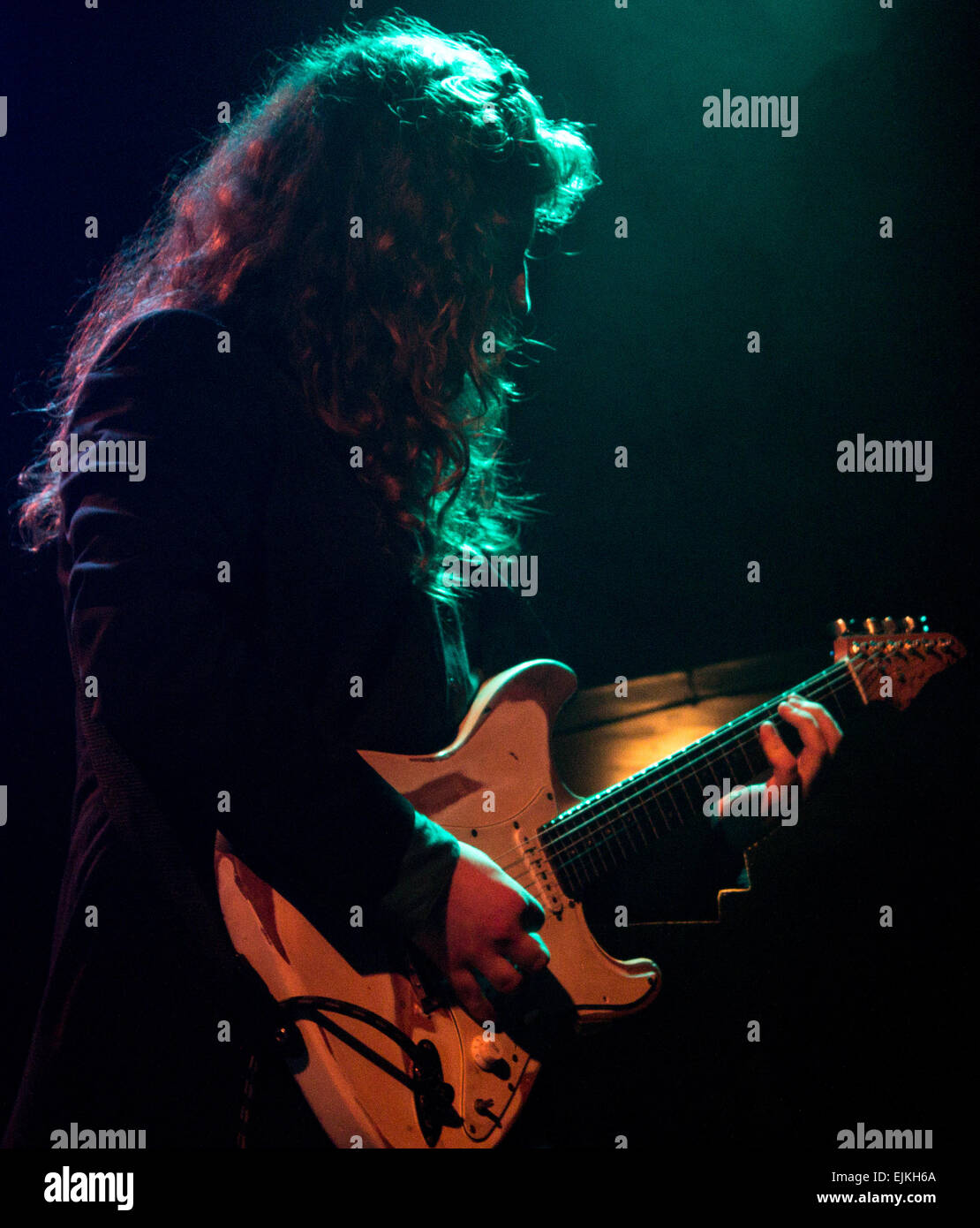 Side profile of a man playing a guitar on stage with the light ...