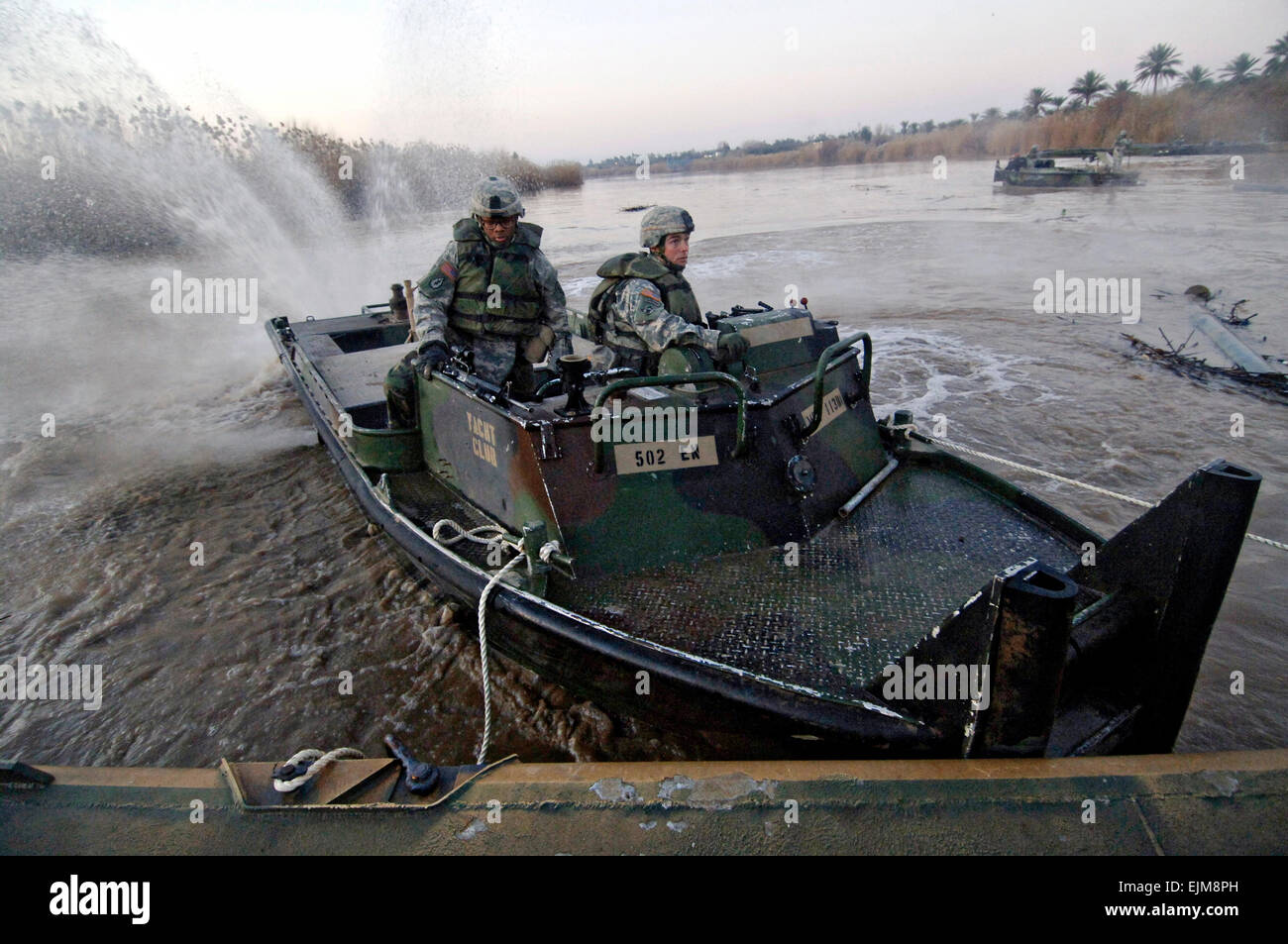 US Army soldiers use a boat to pull a section of floating assault float ...
