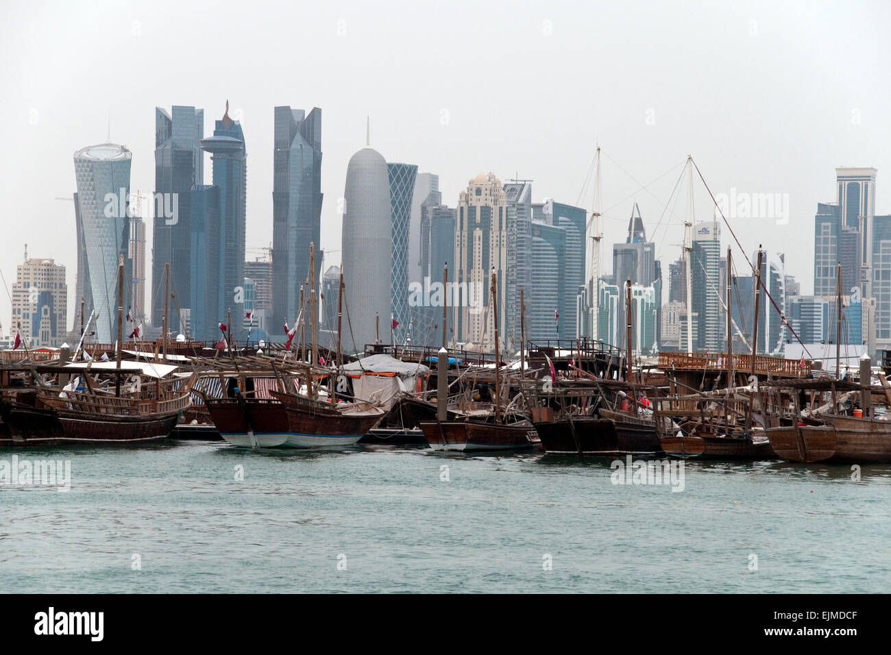 A fleet of dhow boat docked in a port, with the skyline of Doha, Qatar ...