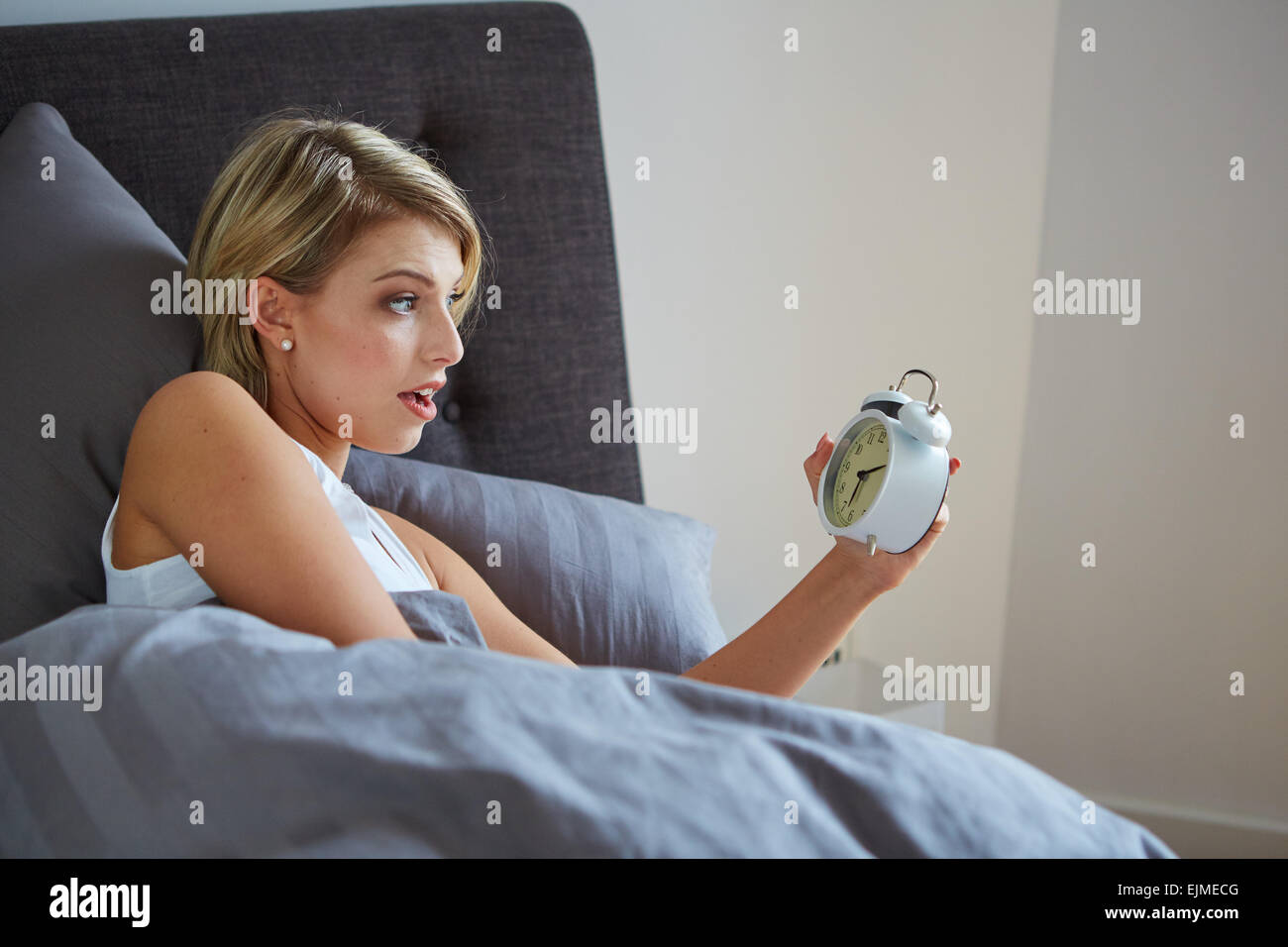 Surprised woman looking at alarm clock Stock Photo - Alamy