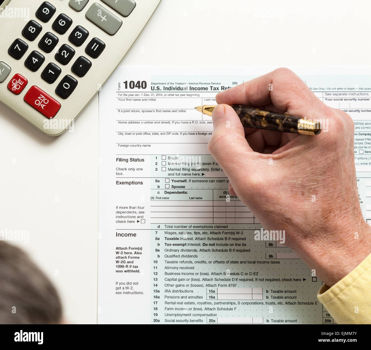 Male caucasian hand holding pen above USA tax form 1040 for year 2014 ...