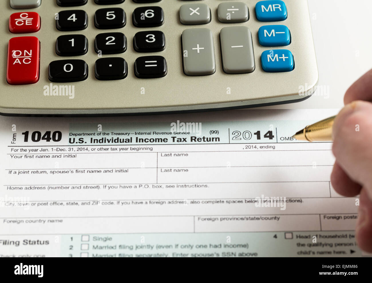 Male caucasian hand holding pen above USA tax form 1040 for year 2014 ...