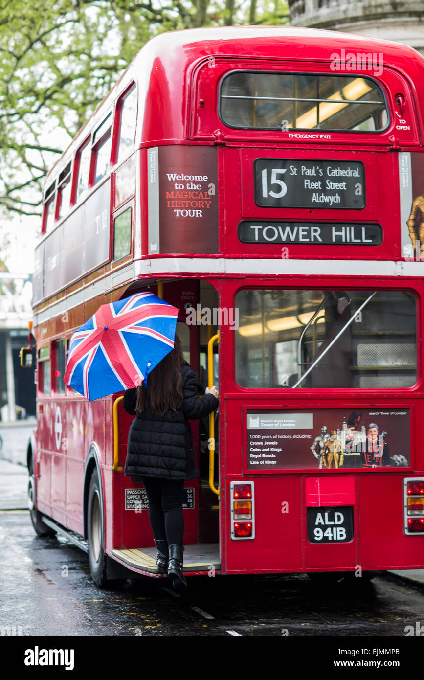 Woman with Union Jack umbrella stepping on to red double-decker bus ...