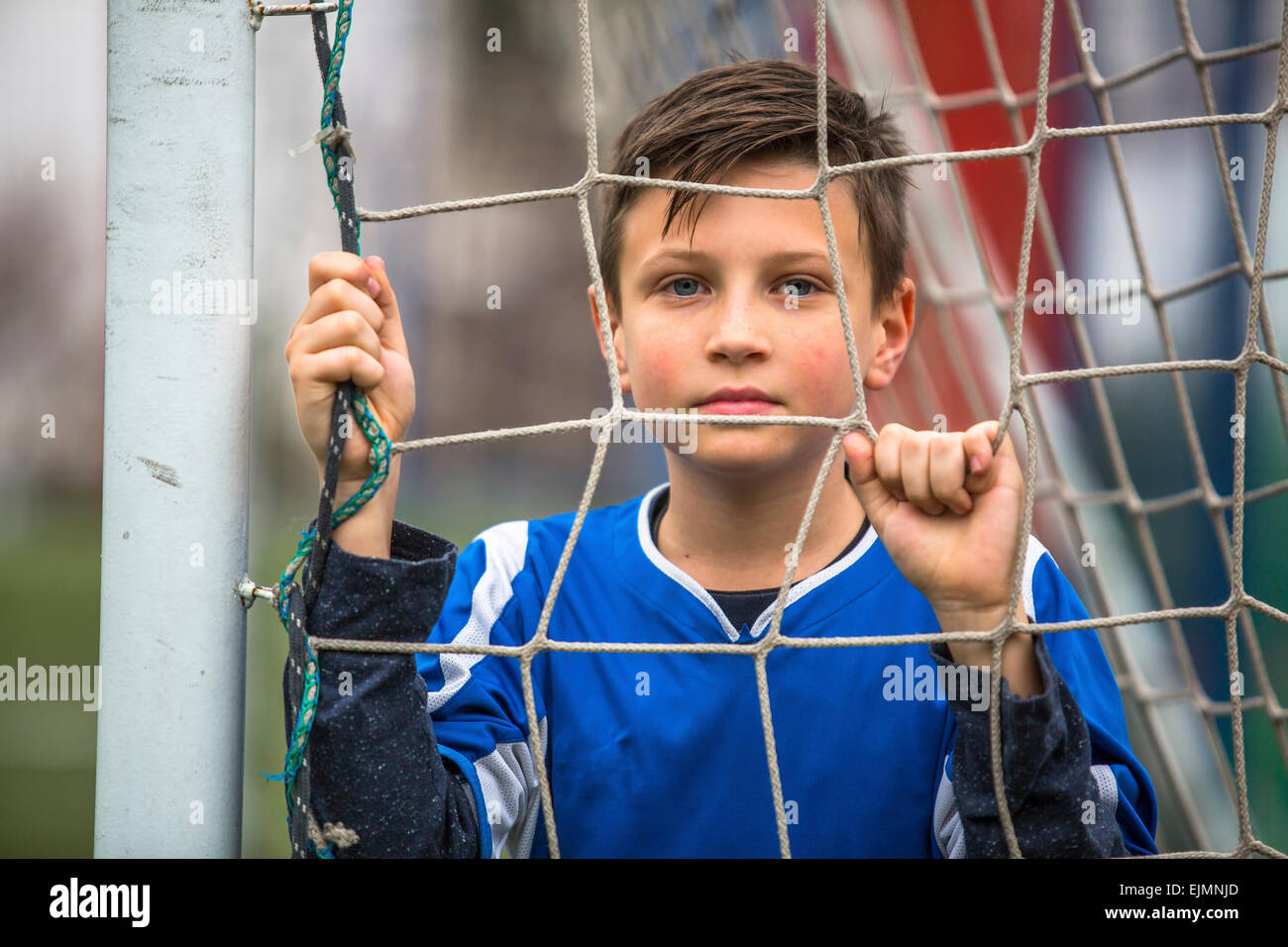 Portrait of a little boy in goalkeeper uniform behind mesh football ...
