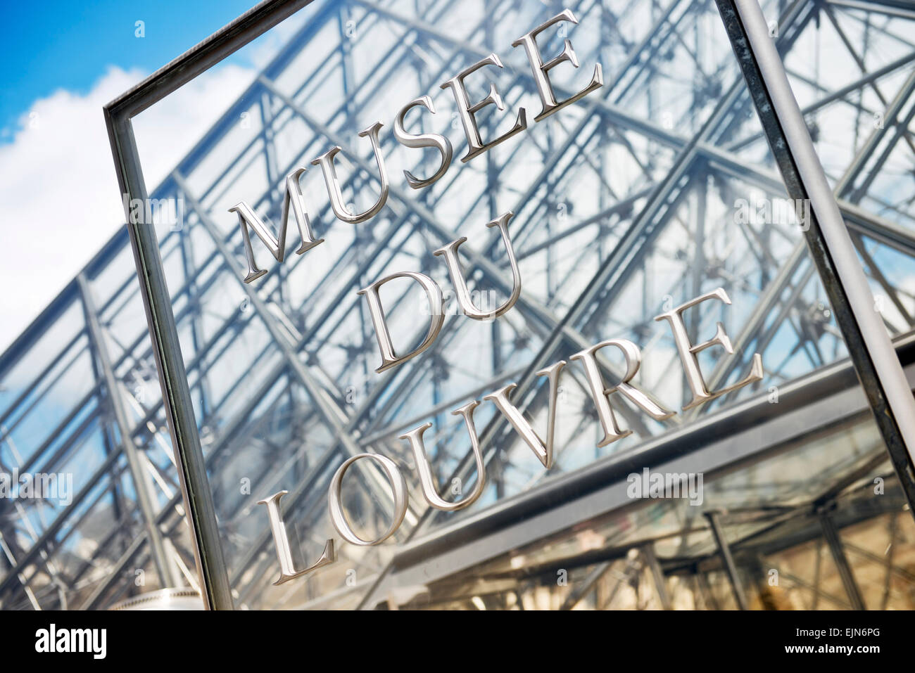 Entrance sign at the Louvre Museum with part of the famous pyramid in ...