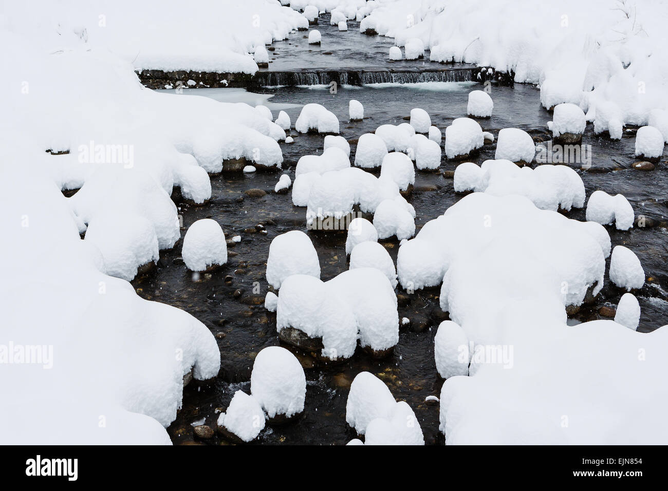 Snow caps on boulders in the mountain river formed after heavy snowfall ...