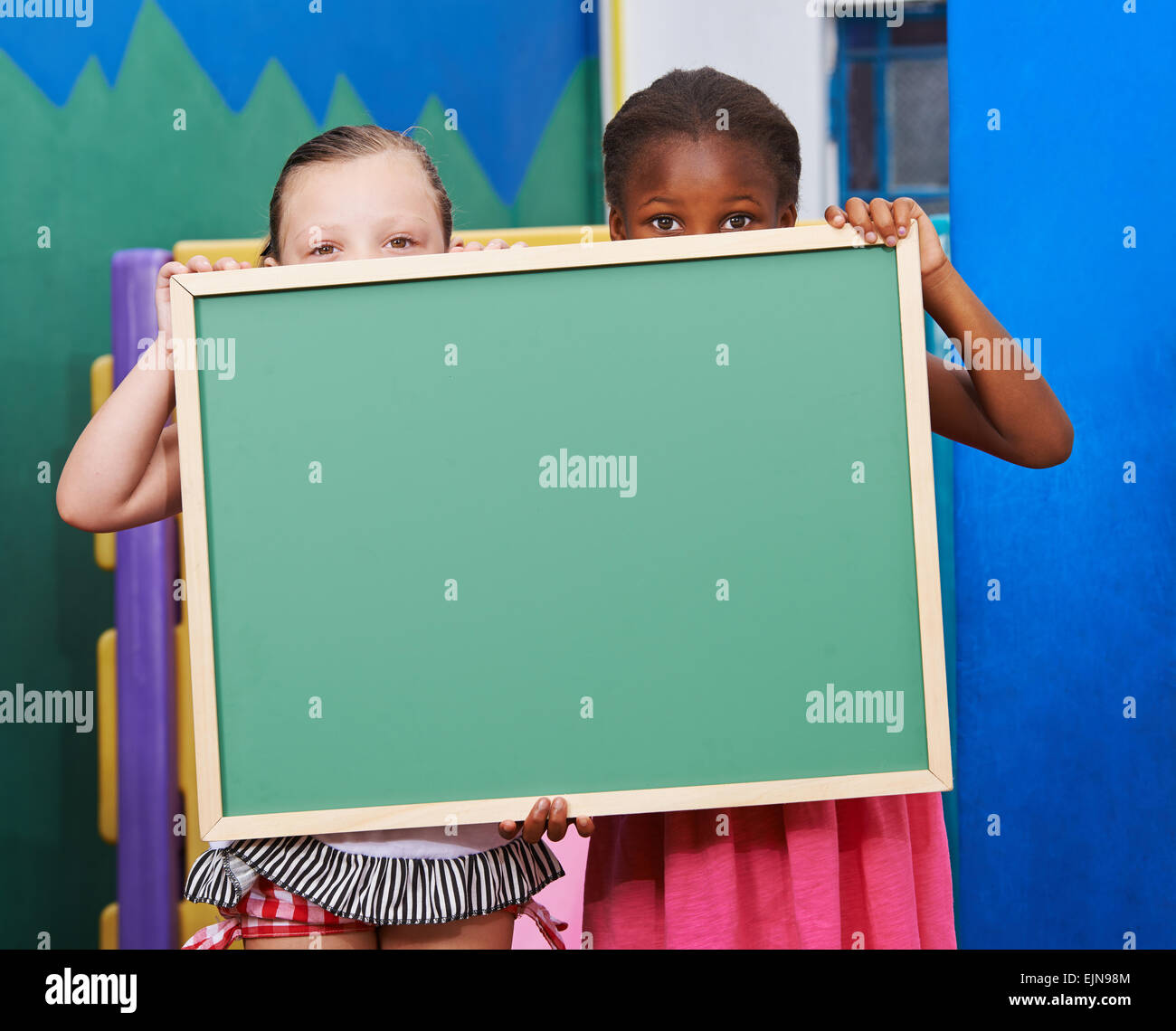 Two children hiding behind an empty chalkboard in kindergarten Stock ...