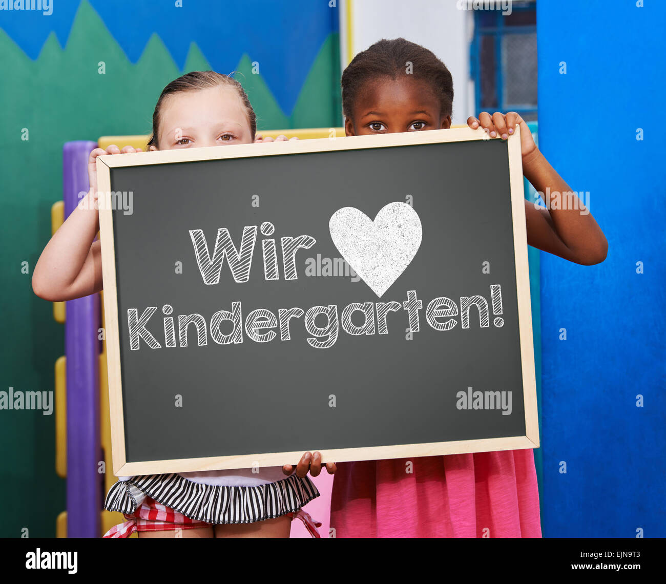 Children holding blackboard with German slogan "Wir lieben Kindergarten ...