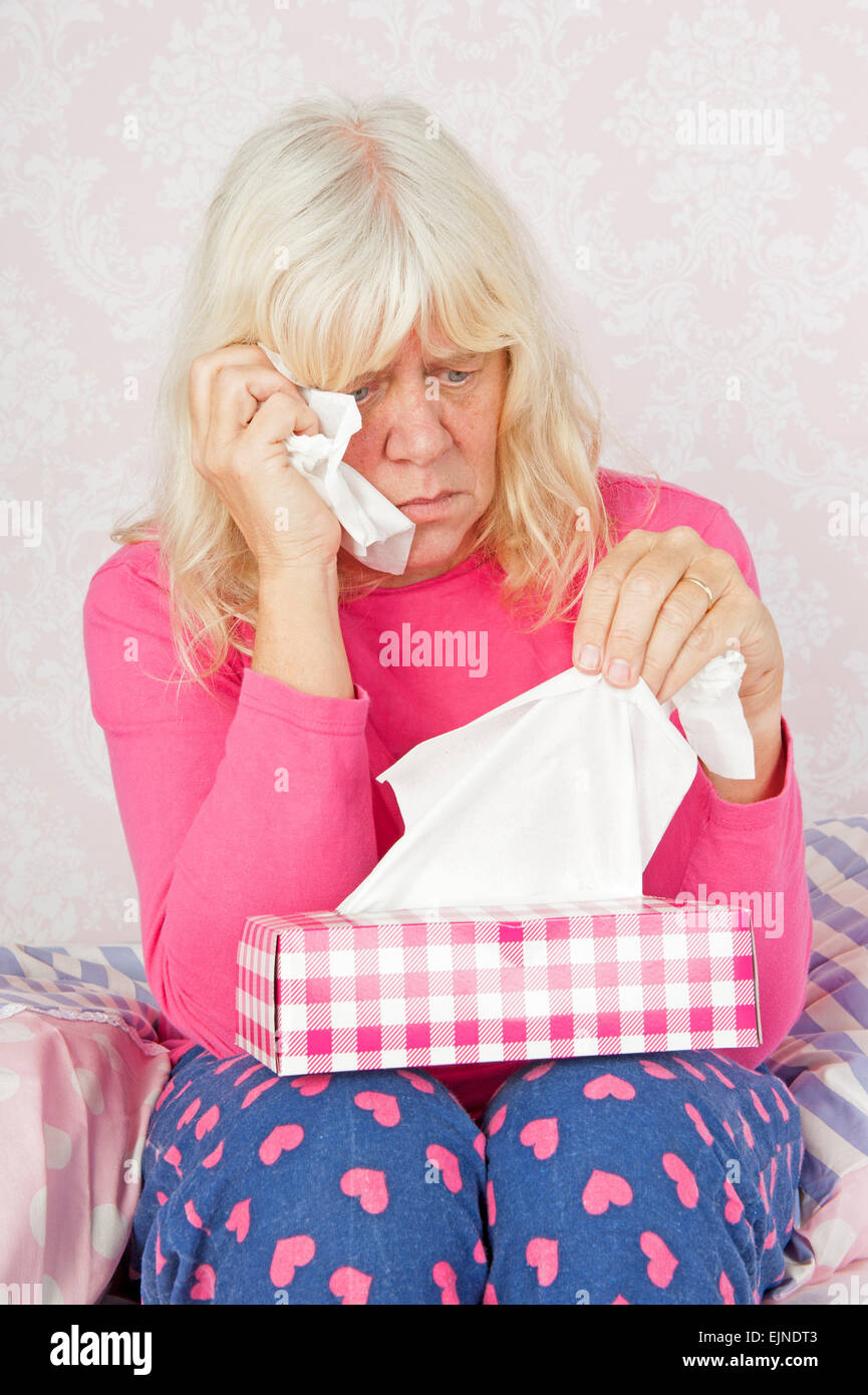 Sad Woman With Pink Pajama And Tissues Sitting On Floor Against Bed
