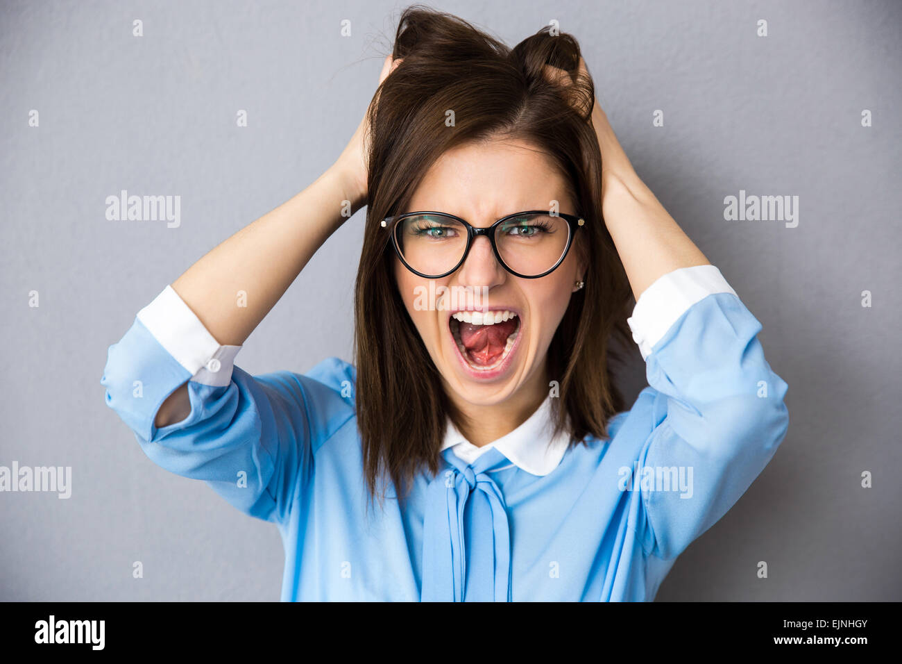 Angry businesswoman touching her hair and screaming over gray ...