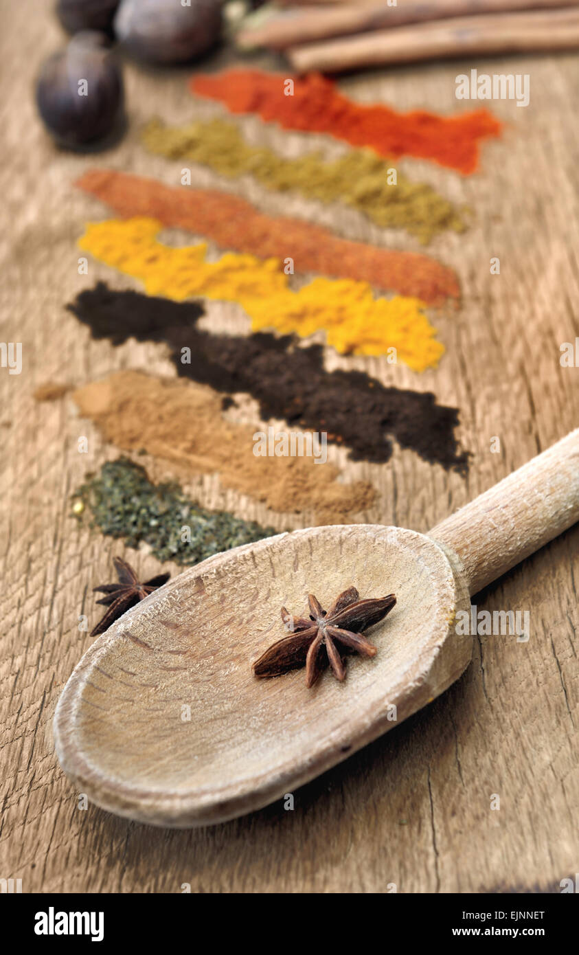 bands of different spices powder, anise in spoon on wood background ...