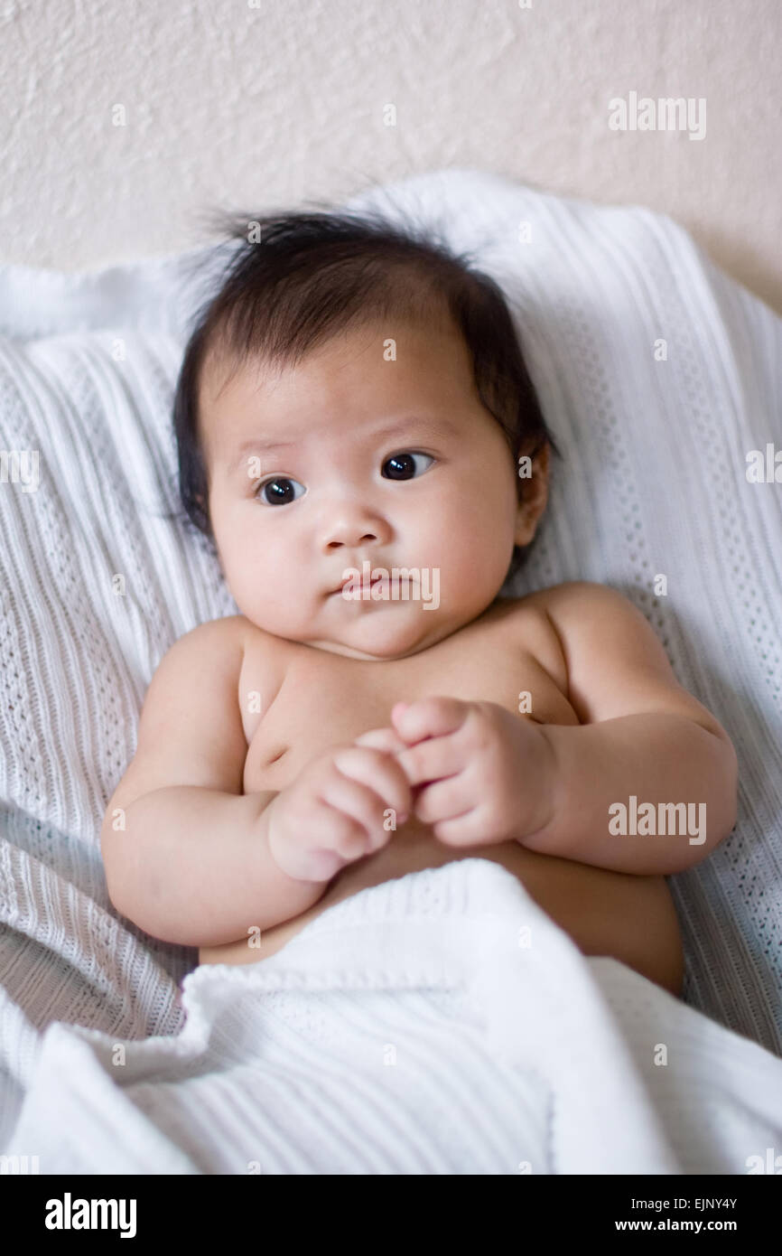 Close up of baby leaning in bed, hands together and looking away from ...
