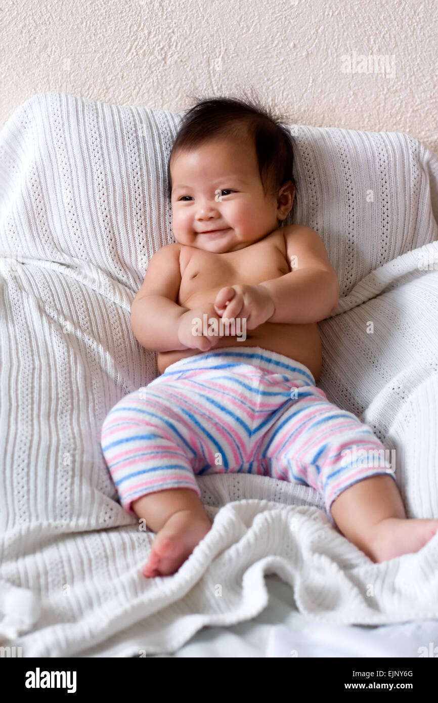 Full body shot of smiling baby in pajamas leaning in bed, hands ...
