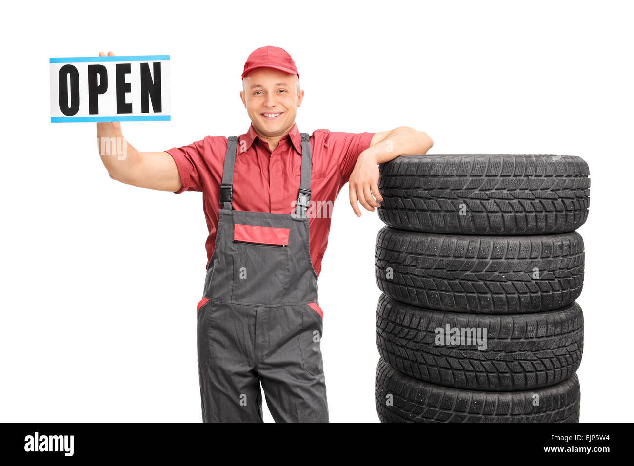 Cheerful mechanic holding an open sign and standing next to a stack of ...