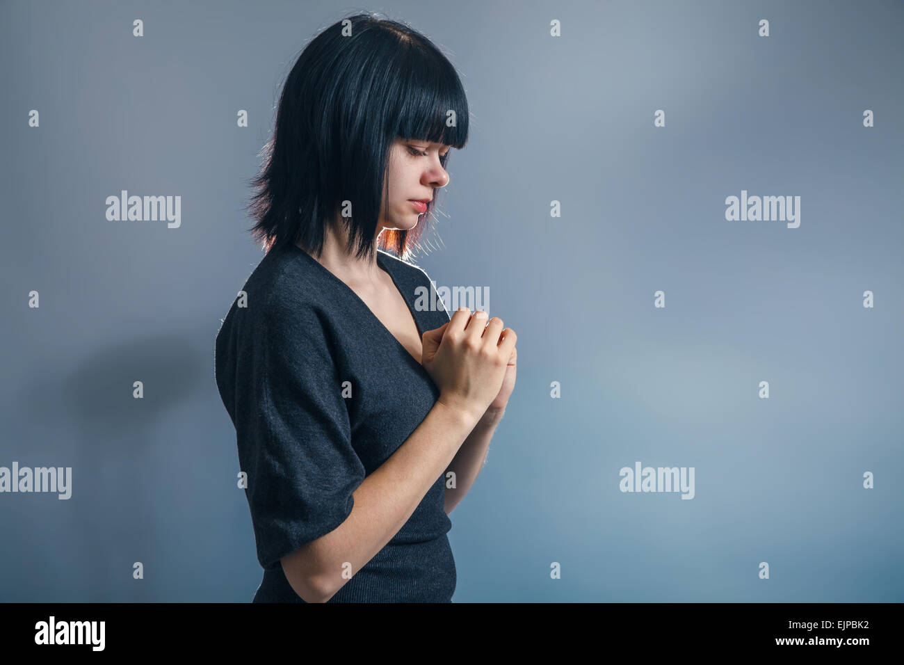 European-looking girl brunette in black jacket folded hands pray Stock ...